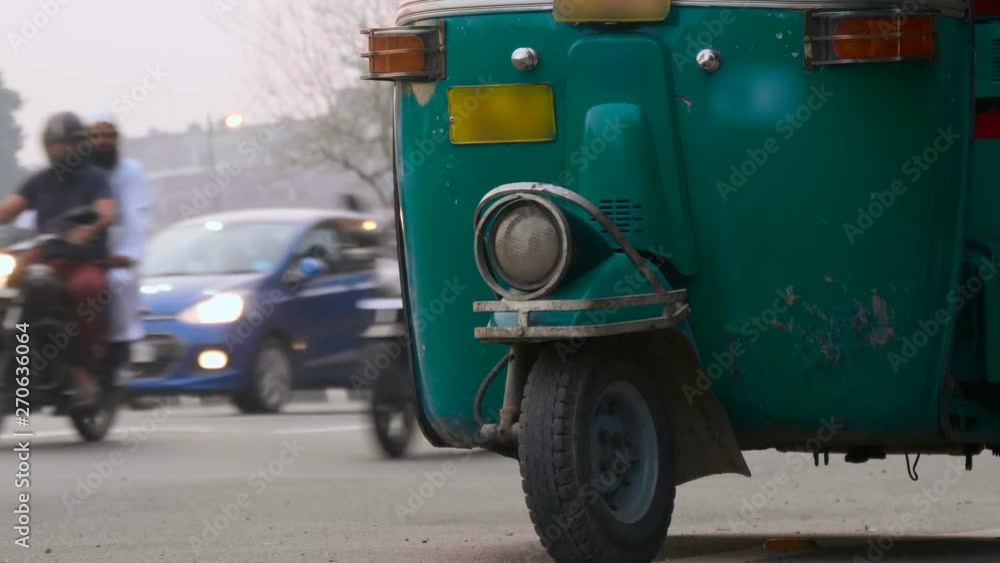 Motor-rickshaw of green color stands on the edge of the road, waits for ...