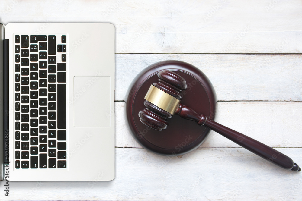 Laptop next to a judge hammer on a white wooden desktop. From above ...