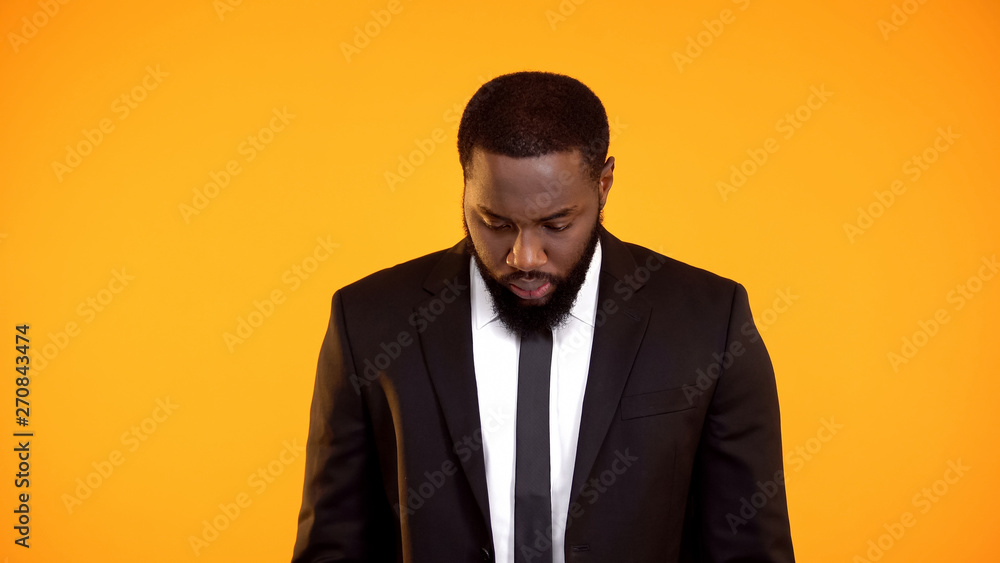 Black man in formalwear looking down feeling guilty, thinking about ...