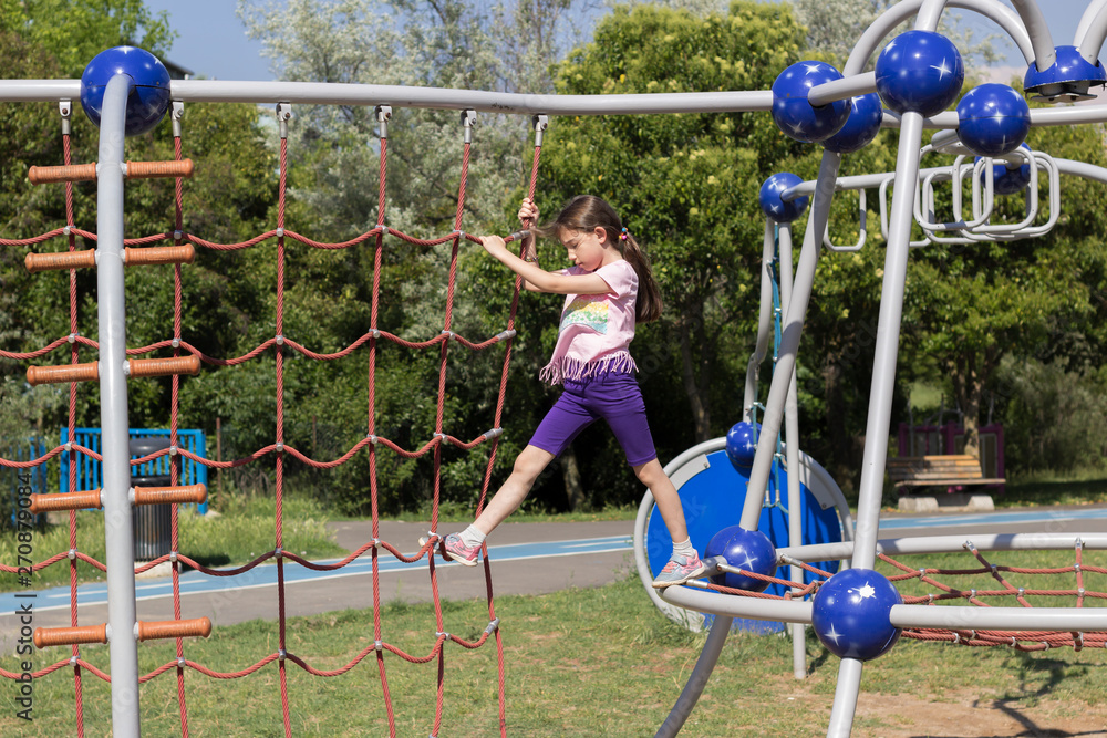 Girl climbing on the rope wall at the playground on spring and summer ...