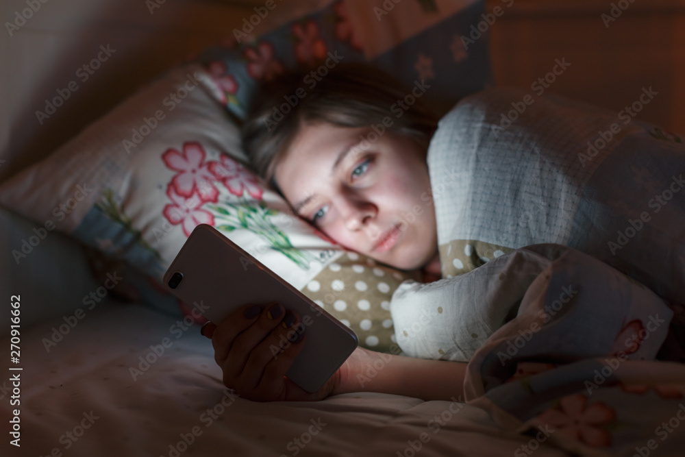 Young sleepy tired woman lying in bed using smartphone at late night ...