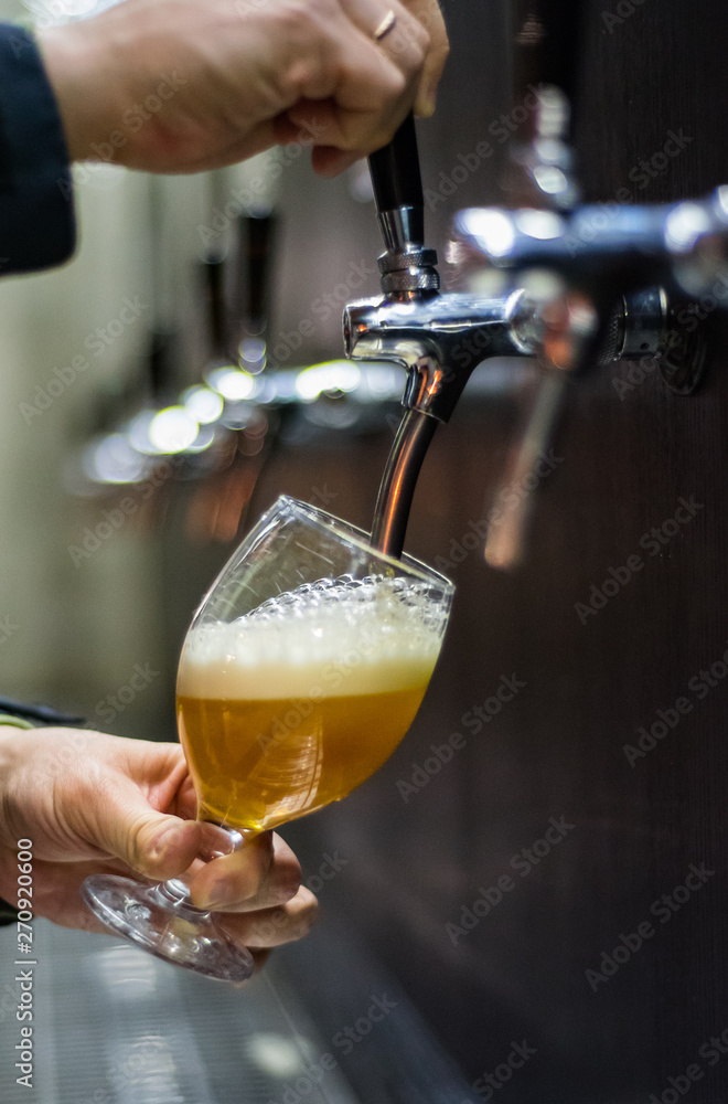 bartender hand at beer tap pouring a draught beer in glass serving in a ...
