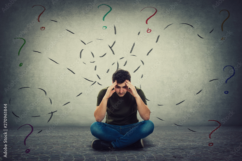 Confused and tired young man seated on the floor keeps hands to ...