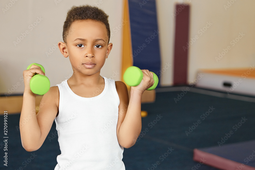 Cute boy athlete of African appearance doing physical exercises at gym ...