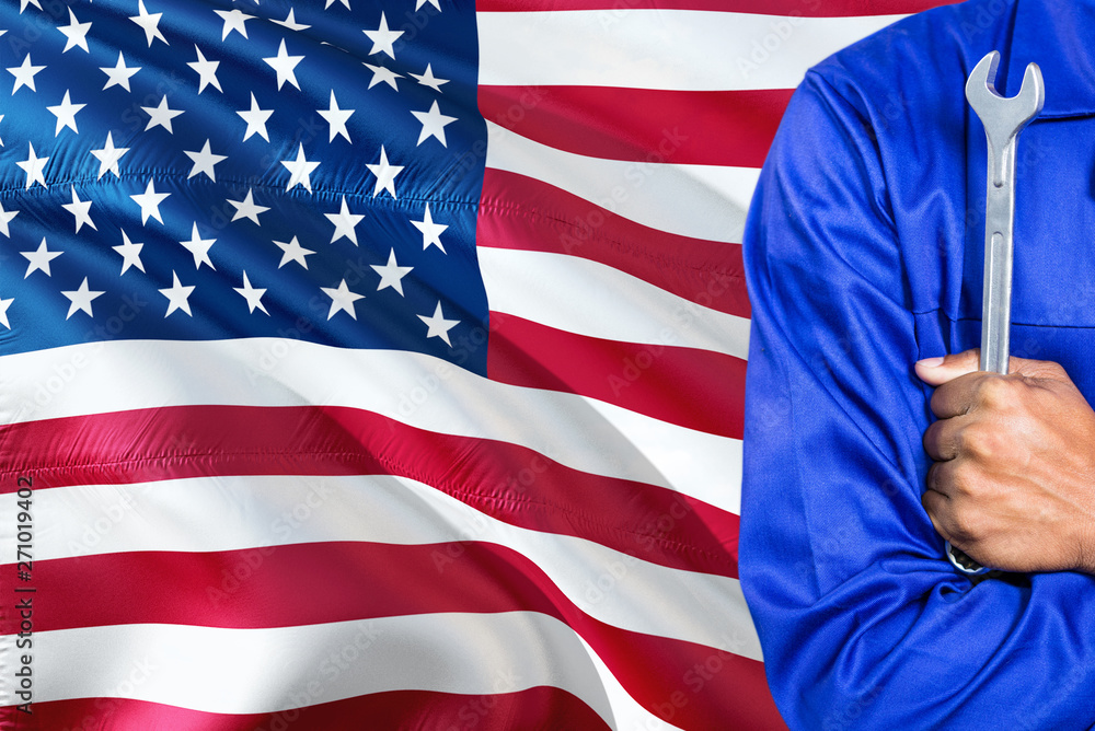 American Mechanic in blue uniform is holding wrench against waving ...