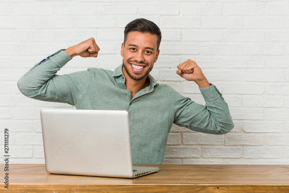 Young filipino man sitting working with his laptop showing strength ...