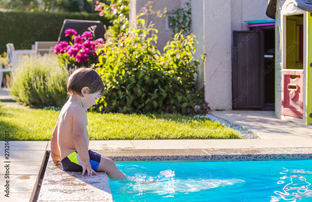 Little happy boy sitting on side of swimming pool in garden playing by ...