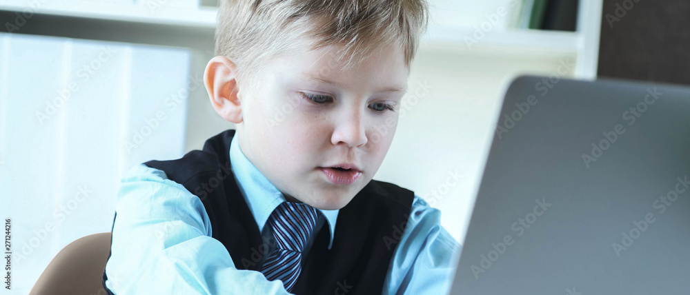 Small cute boy in business suit with a tie works at computer at office ...