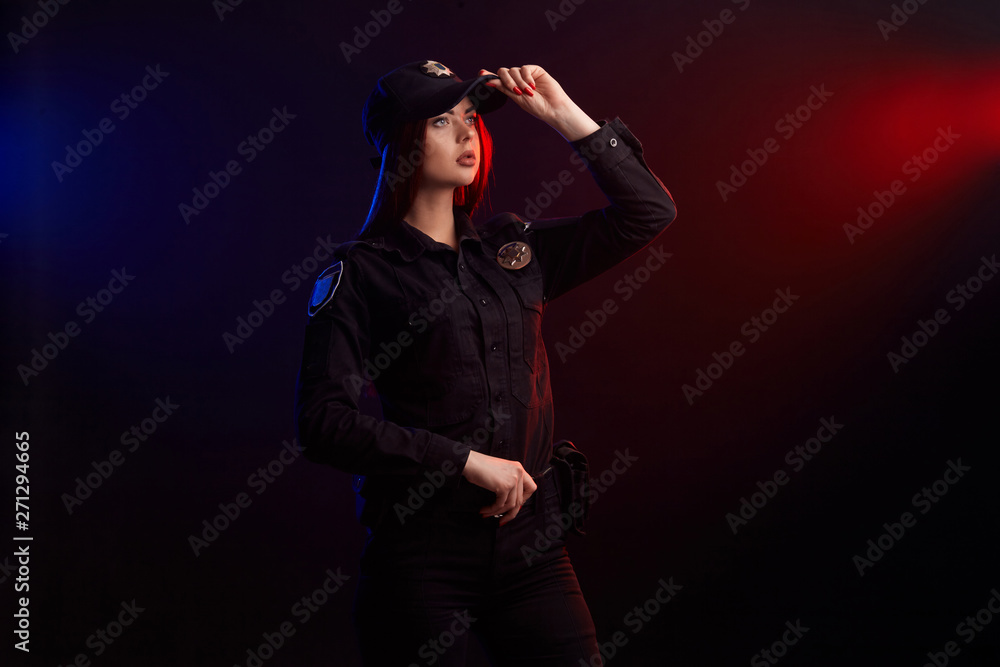 Serious female police officer is posing for the camera against a black ...