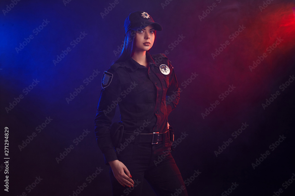 Serious female police officer is posing for the camera against a black ...