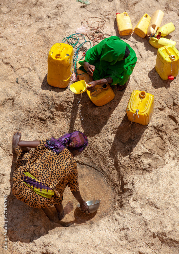 Somali women taking drinking water from a well hole in the sand and ...
