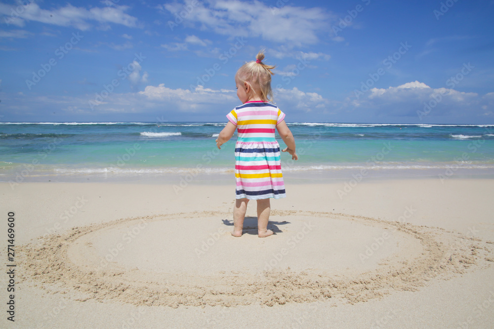 Back view of playful toddler girl on the white sandy beach looking at ...