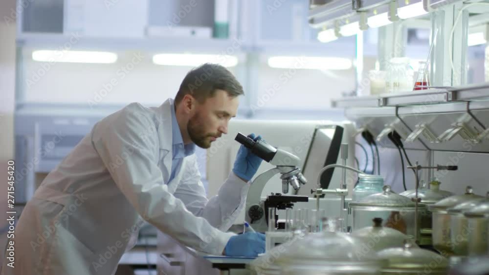 Medium shot of male researcher in medical gown leaning on desktop in ...