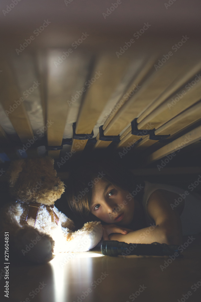 Little child, hiding under the bed, hugging teddy bear and holding ...