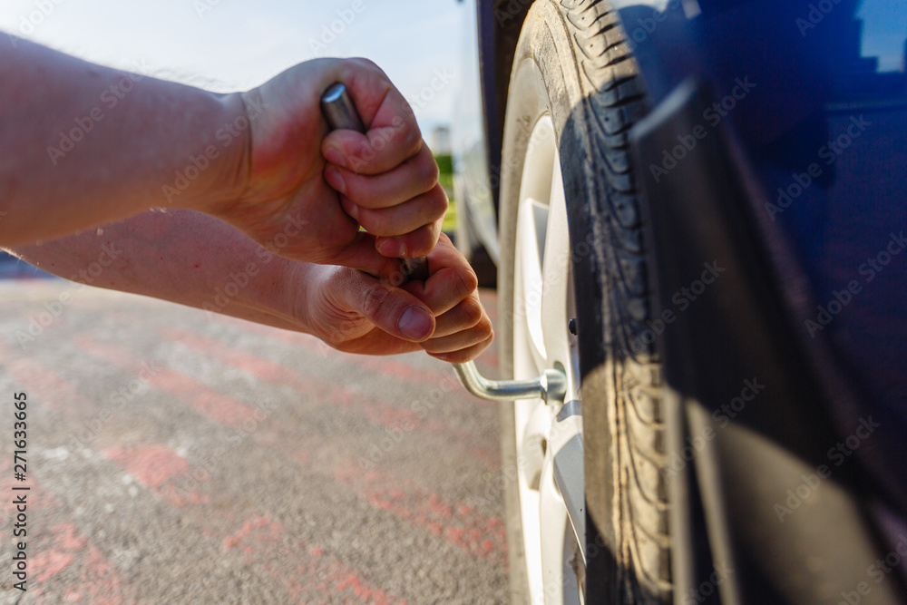 Close-up hands with cylinder wrench unscrew damaged wheel of car. Man ...