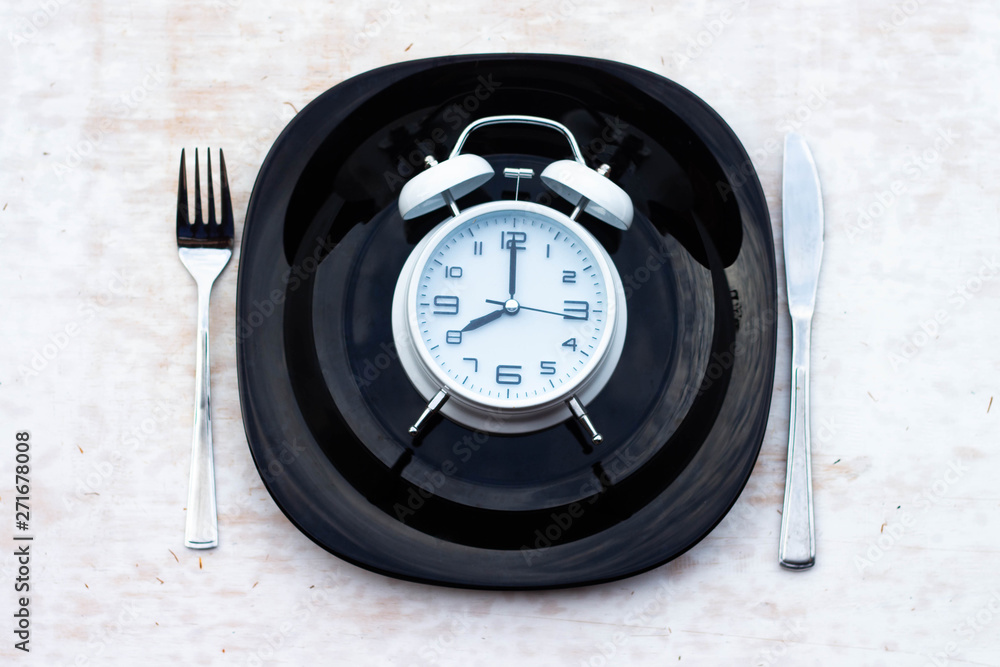 Concept of breakfast time with white alarm clock, black plate, fork ...