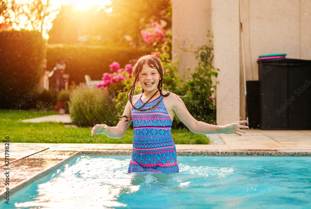 Happy preteen girl having fun in swimming pool splashing water drops ...