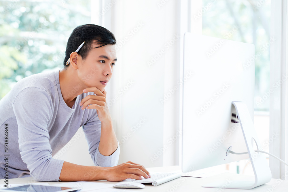 Foto de Pensive young Vietnamese ui designer with pencil behind his ear ...