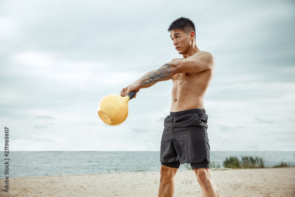 Young healthy man athlete doing exercise with the weight at the beach ...