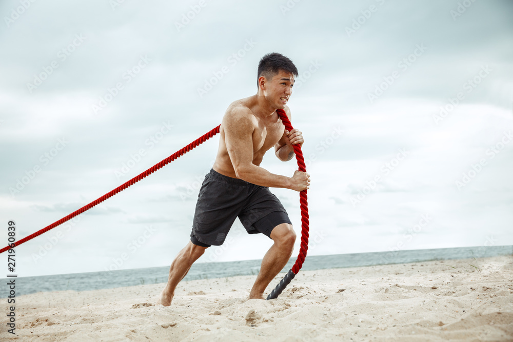 Young healthy man athlete doing exercise with the rope at the beach ...