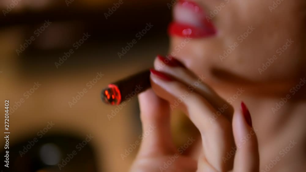 close-up. female lips. gorgeous woman with red lipstick on her lips and with a cigar on a dark ...