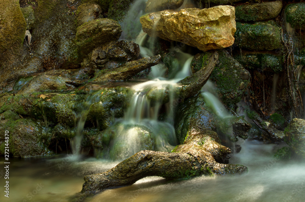 Small waterfall and stream of water among rocks and boulders and fallen ...