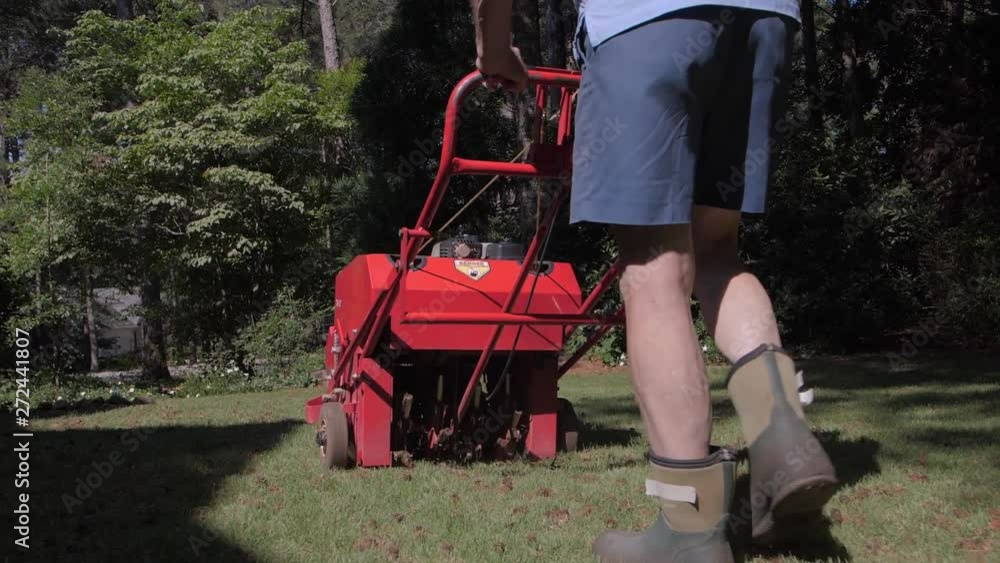 Man using gas powered aerating machine to aerate residential grass yard ...