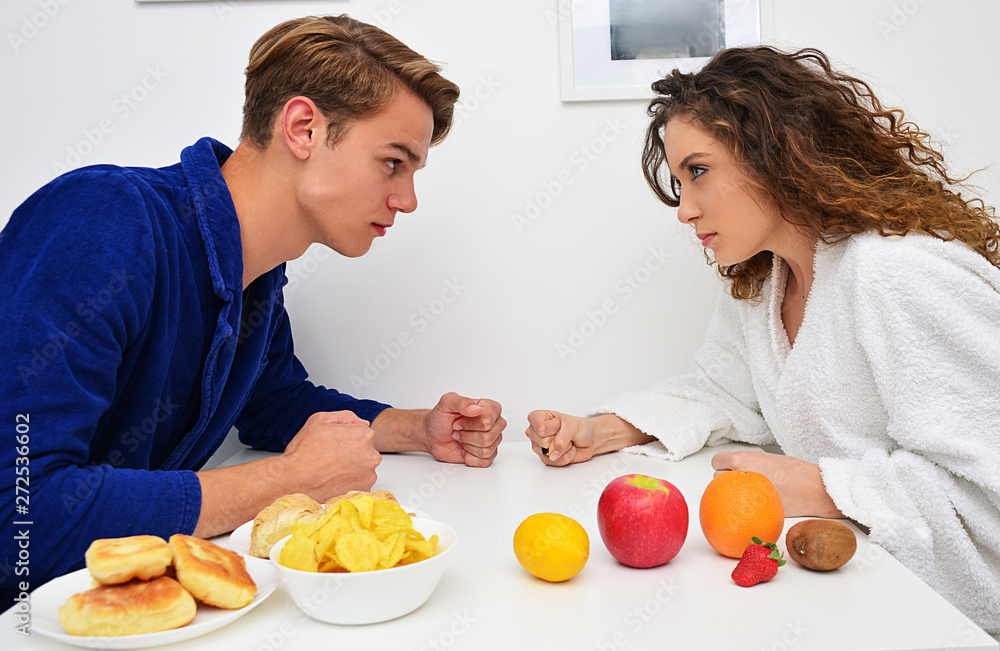 young couple sitting at table arguing over healthy and unhealthy meal ...