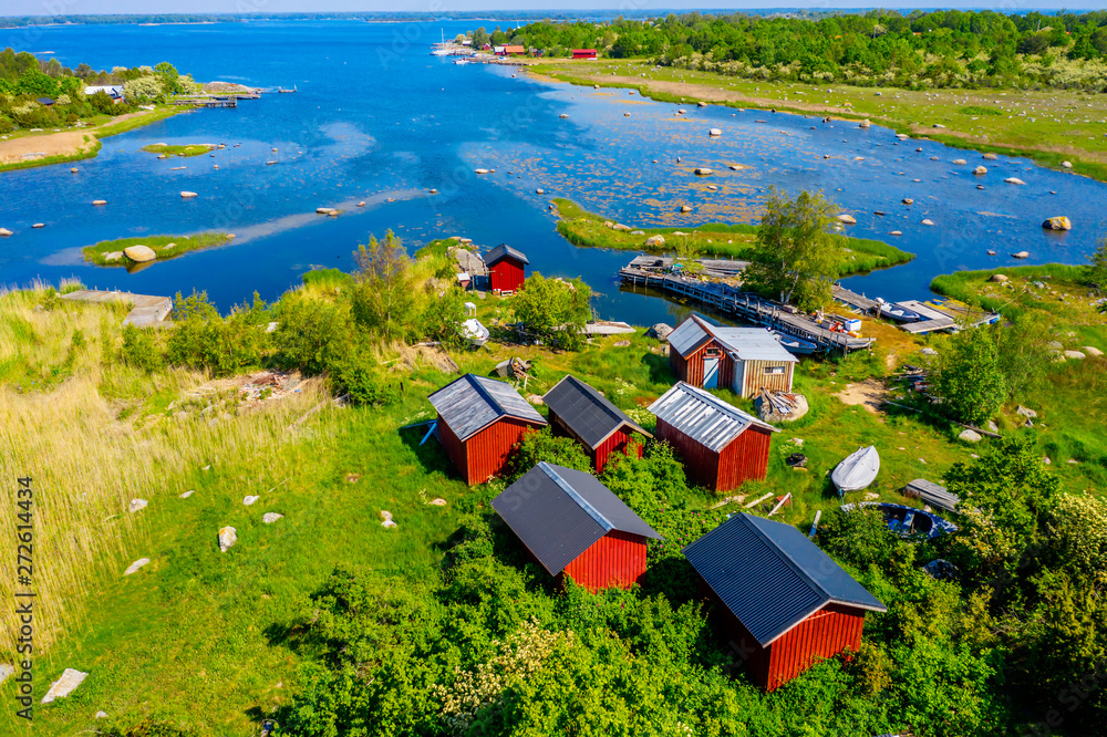 Small red fishing sheds among shrubs at the end of a shallow bay ...