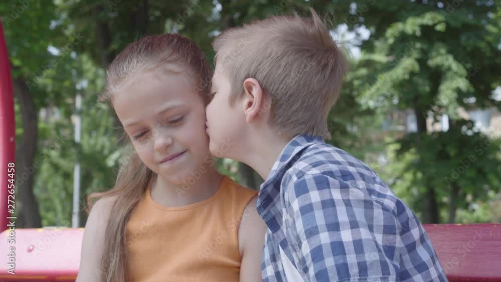 Portrait of adorable blond boy kissing cheek of a pretty girl sitting ...