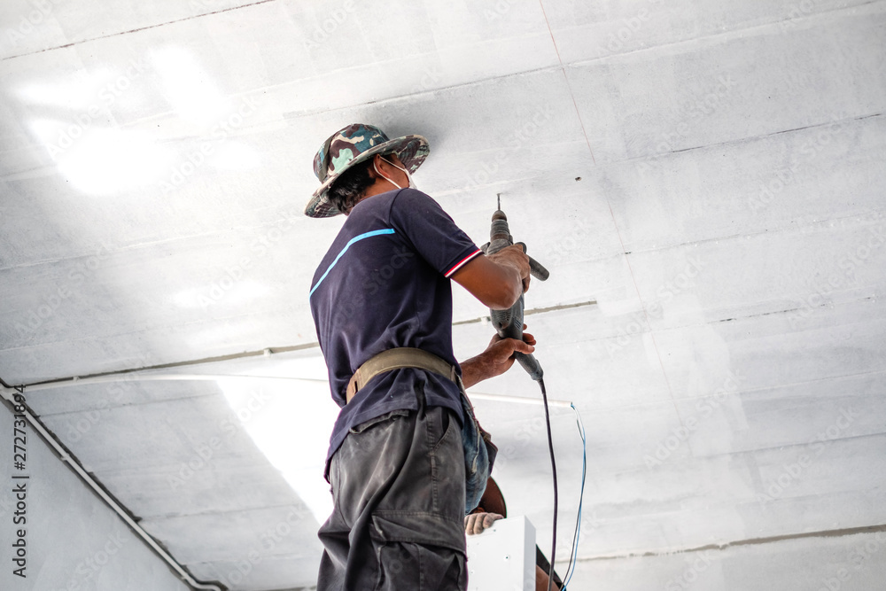 Worker is drilling holes on the ceiling with electrical screwdriver ...