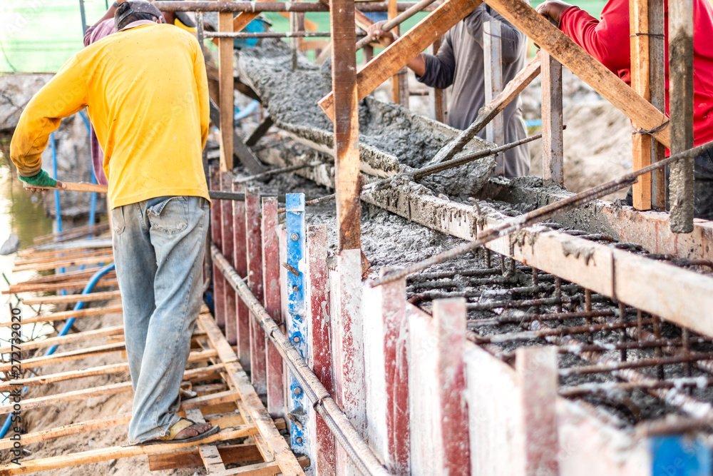 Group of construction workers spreading poured concrete for bridge ...