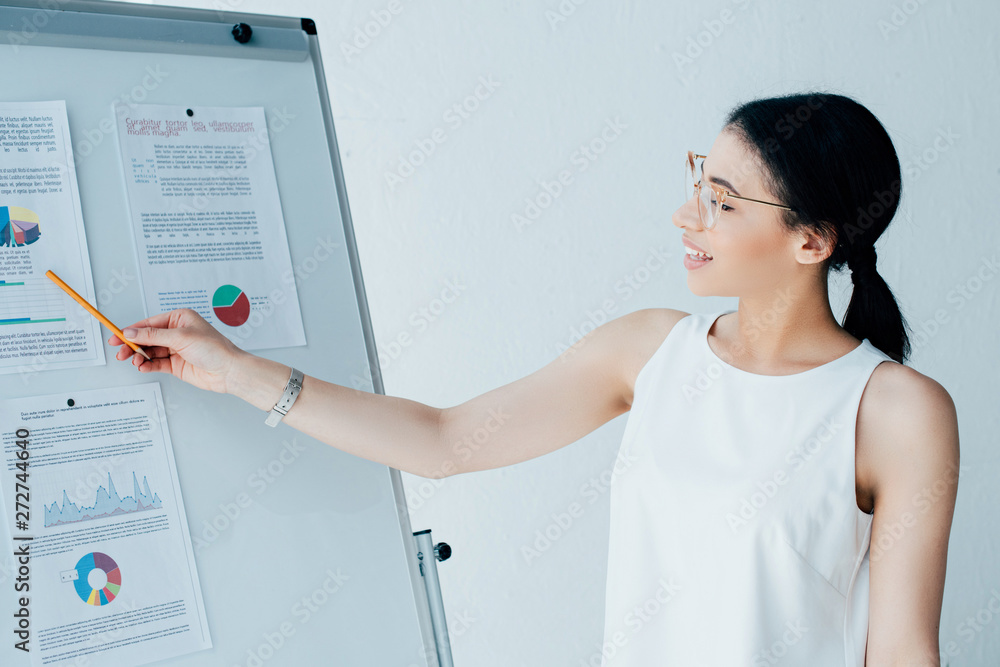 pretty businesswoman pointing with pencil at flipchart with ...