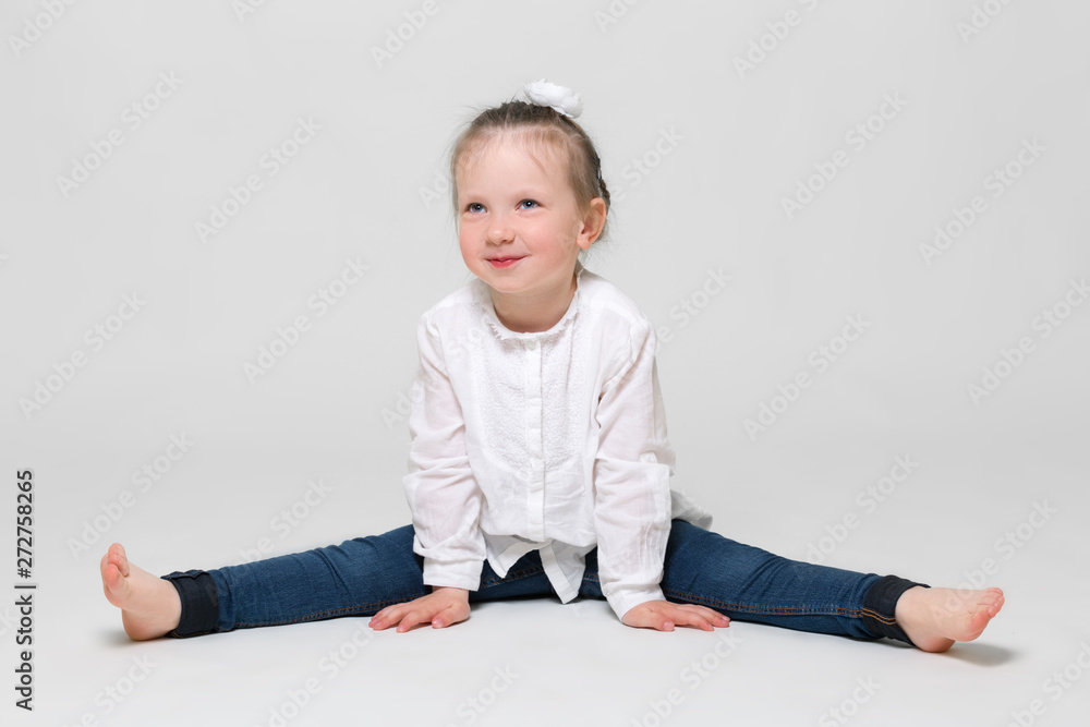 Little girl sits with her legs spread and leans her hands on floor. She ...