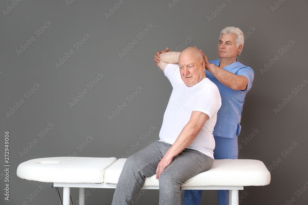 Mature physiotherapist working with senior man on grey background Stock ...