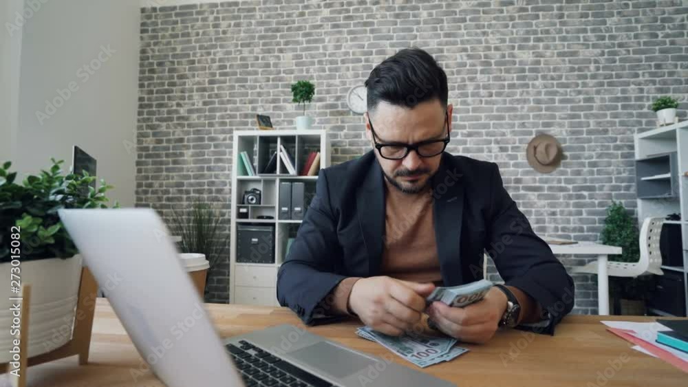 Rich entrepreneur handsome brunet in glasses is counting money smiling ...