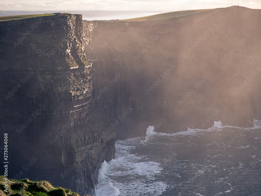Ocean wave at the bottom of Cliff of Moher, Mist in the air. Tourist on ...