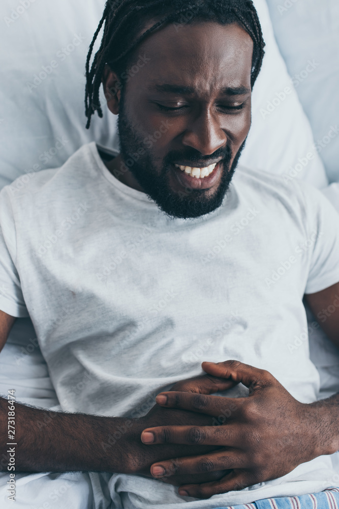 exhausted african american man suffering from stomach pain in bedroom ...
