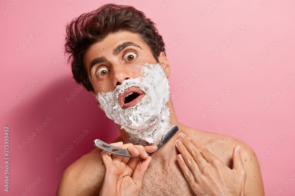 Shocked young man applies foam, prepares for trimming beard, holds ...