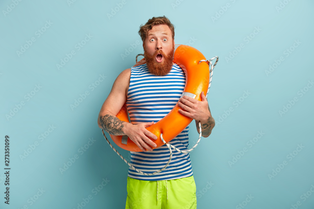Impressed shocked red haired lifeguard works at beach, uses lifebuoy ...