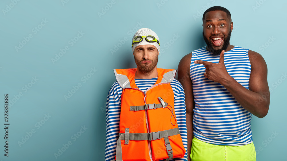 Positive dark skinned man points at sad gloomy lifeguard who wears ...