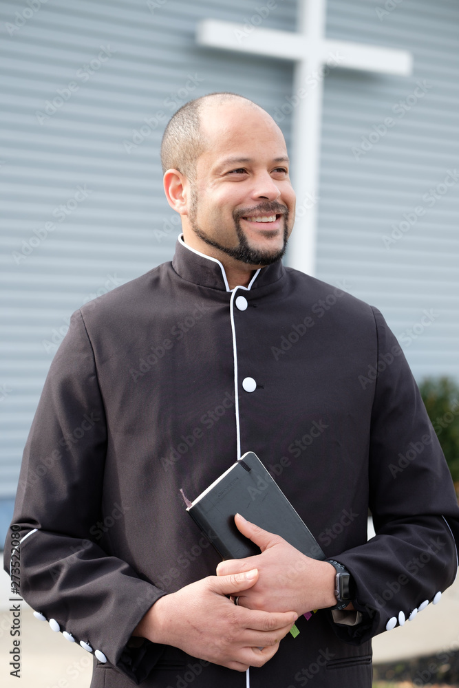 A african-american Male Reverend stands in front of a church with a ...