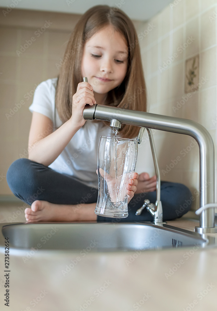 Pouring water into a glass. A little caucasian girl pours water from a ...