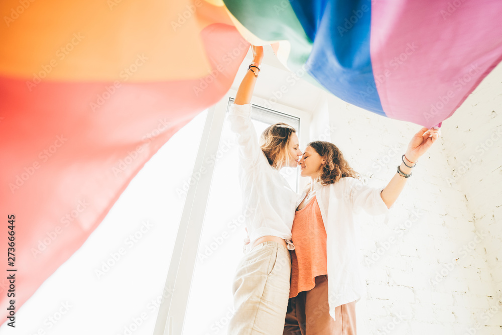 Beautiful female young lesbian couple in love standing near the window ...
