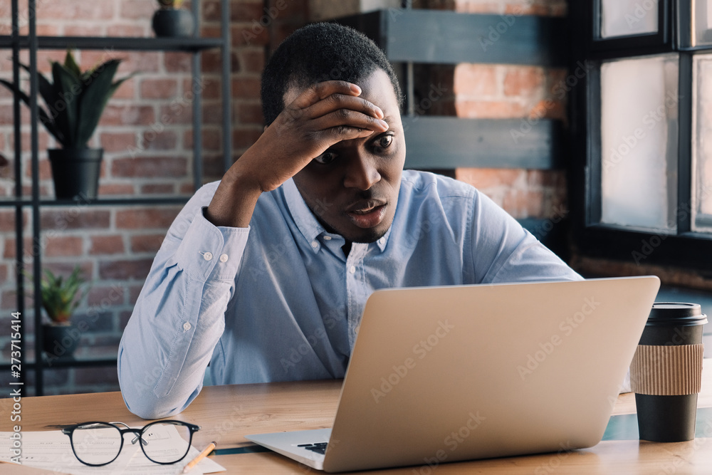 Frustrated african american business man sitting at his desk in modern ...