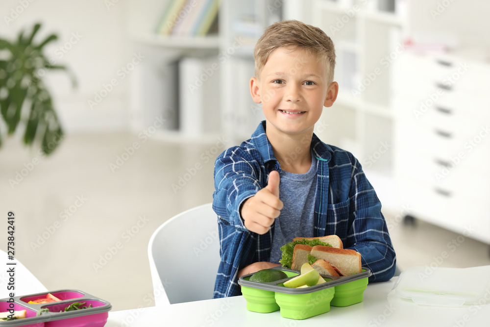 Little schoolboy with tasty lunch in box showing thumb-up gesture in ...