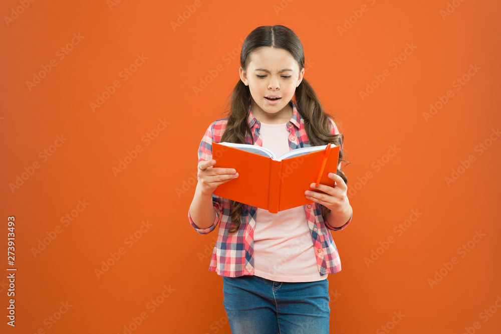 Shes a true bookworm. Adorable small child reading book on orange ...