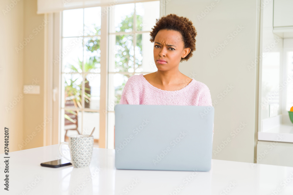 Young african american woman working using computer laptop skeptic and ...