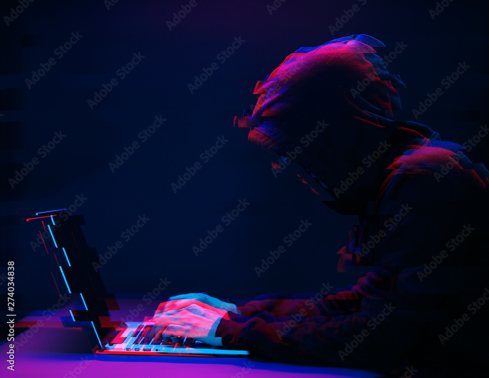 Hacker in the hood working with laptop typing text in dark room. Image ...