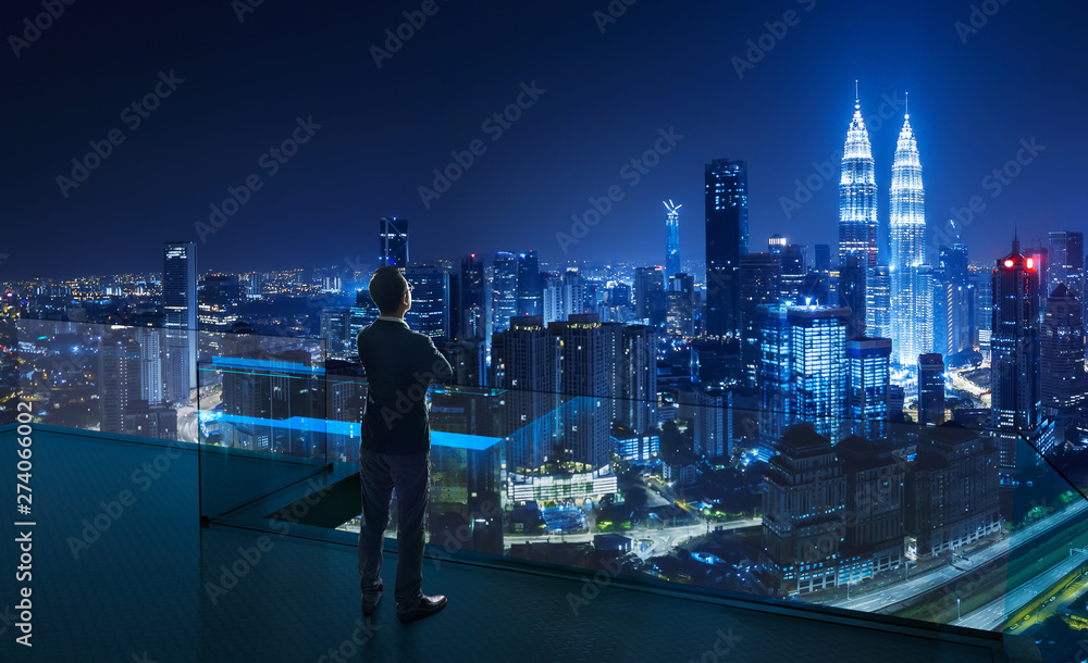 Businessman standing on open roof top balcony watching city night view . Business ambition and ...